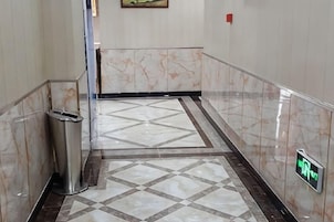 Um corredor com piso estampado, uma lixeira e um aviso de saída de emergência fixado na parede.