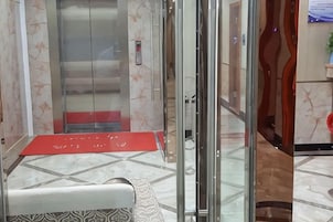 Um saguão de hotel com elevador de vidro, piso estampado e tapete vermelho.