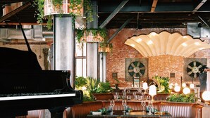Restaurante com piano de cauda, cabines de madeira e parede de tijolos.