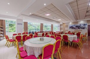 Sala de conferências com mesas e cadeiras redondas, janelas amplas e uma tela de televisão.