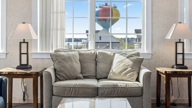 Sala de estar com sofá, duas luminárias, uma mesa e janela com vista para uma torre d'água colorida.