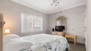 Quarto com cama, escrivaninha, televisão e espelho.