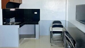 Cozinha compacta com bancada preta, eletrodomésticos de aço inoxidável e um pequeno espaço de estar com uma cadeira e um banquinho.