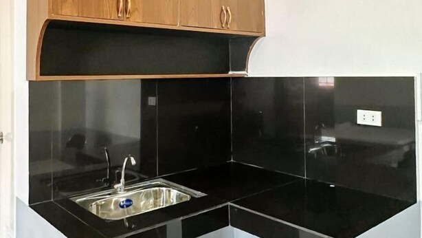 Uma cozinha com bancadas pretas, pia de aço inoxidável e armários de madeira.
