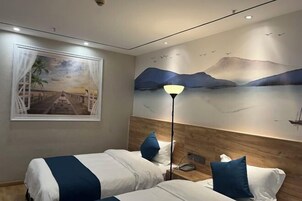 Quarto de hotel com duas camas, uma mesa de cabeceira, uma luminária e um mural com uma cena do pôr do sol.
