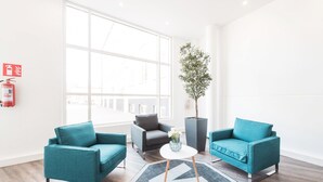 Quarto moderno com poltronas verde-água, uma pequena mesa branca e uma janela grande.