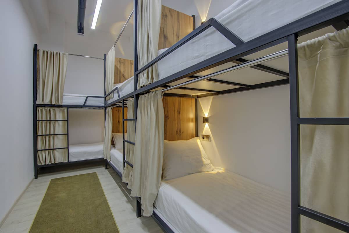 Quarto em dormitório com beliches, tapete verde e luminária na parede.