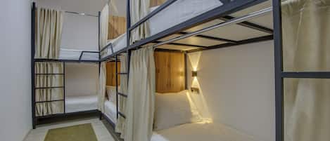 Quarto em dormitório com beliches, tapete verde e luminária na parede.