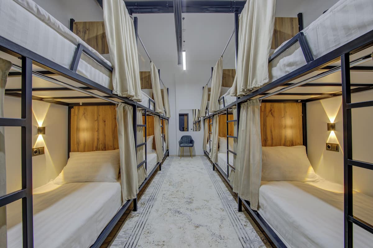 Um corredor com beliches, cabeceiras de madeira e luminárias fixadas na parede.