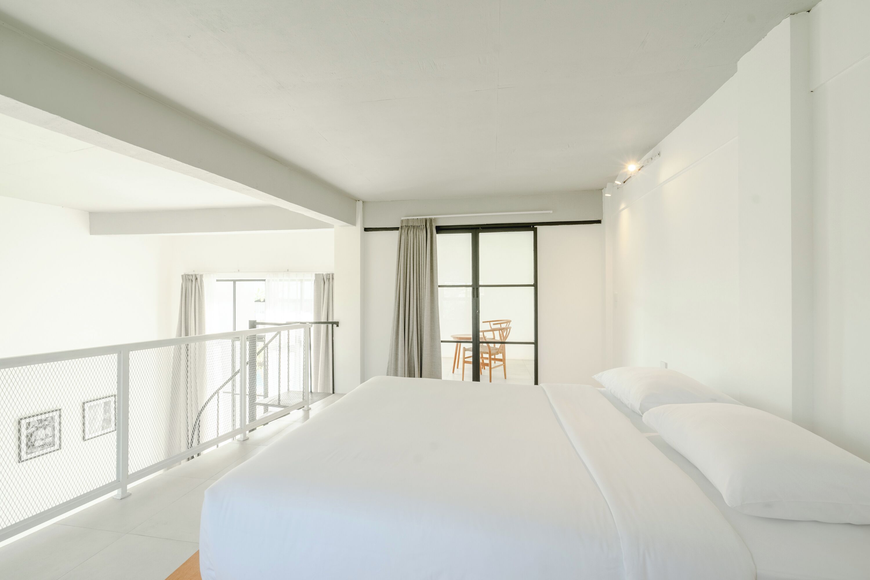 Um quarto espaçoso com uma cama grande, varanda com guarda-corpo e área de jantar com cadeiras e mesa.
