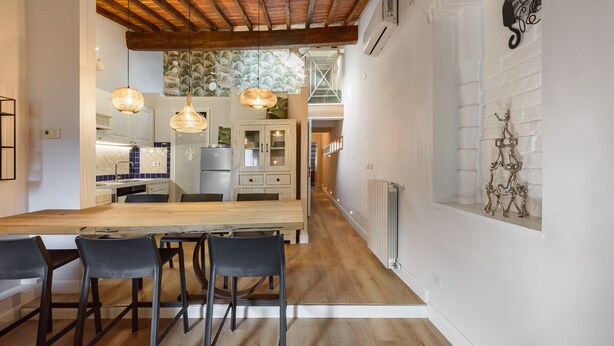 Cozinha moderna com ilha de madeira, banquetas pretas, luminárias pendentes e vista para a sala de estar.