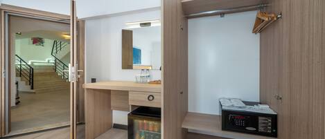 Quarto de hotel moderno com guarda-roupa de madeira, secretária embutida com espelho e minibar.