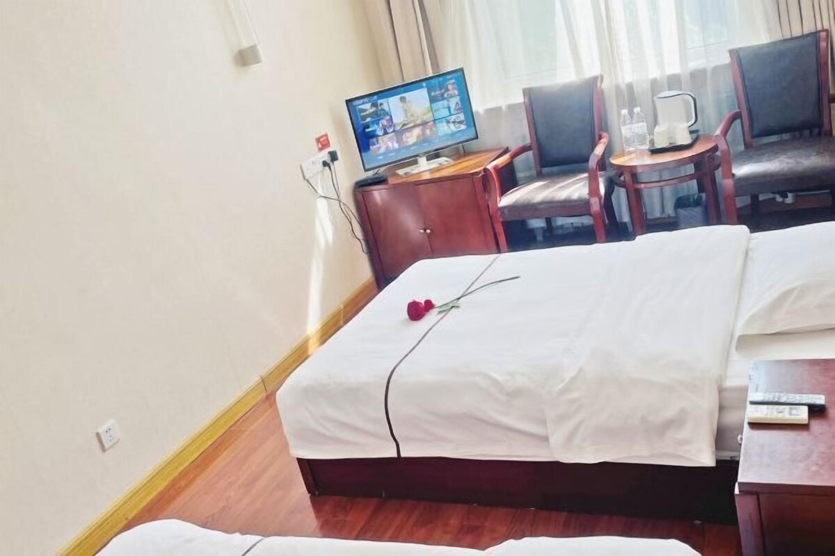 Quarto de hotel com duas camas, televisão, secretária com máquina de café e janela com cortinas.