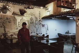 Quarto com painel decorativo, mesas, cadeiras e plantas penduradas.