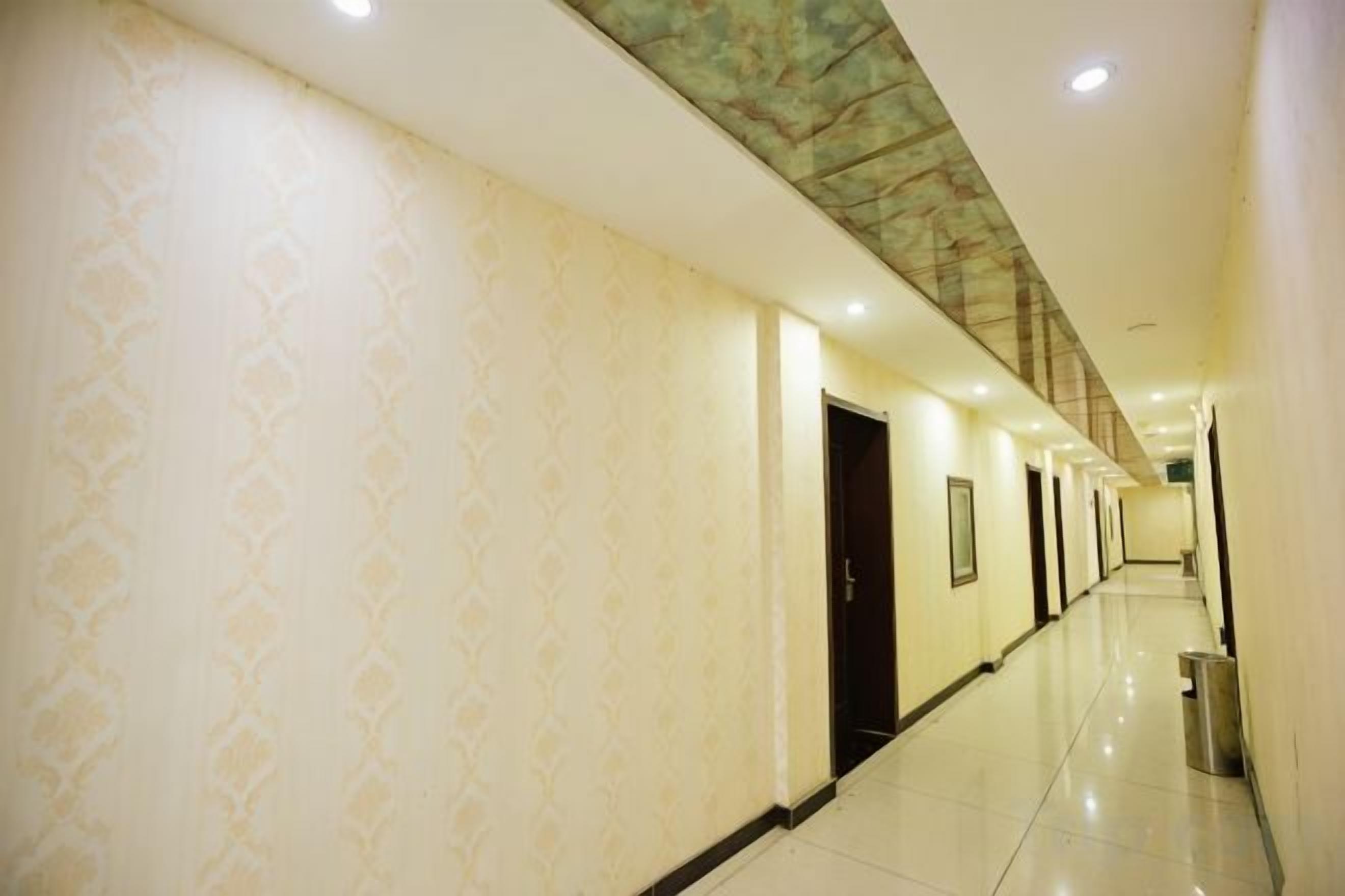 Corredor de hotel com papel de parede estampado, portas e um cesto de lixo.