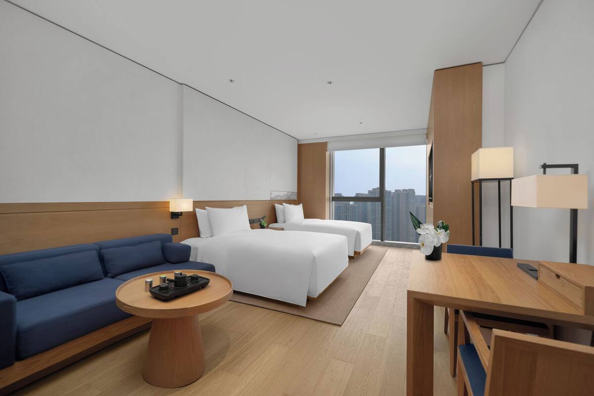 Quarto de hotel moderno com uma cama grande, um sofá, uma escrivaninha e vista para a cidade.