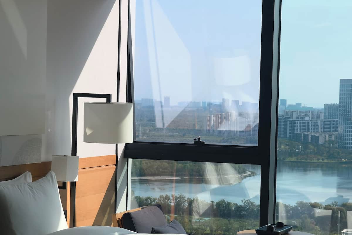 Quarto de hotel com uma janela grande que oferece vista para um horizonte urbano e um rio.