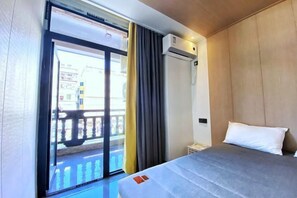 Quarto de hotel com cama, aparelho de ar condicionado e porta de vidro deslizante para área externa.