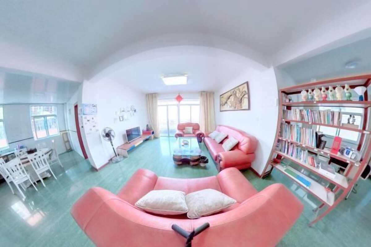 Uma sala de estar com um sofá rosa, uma mesa de centro, uma estante e um espaço de refeições com cadeiras e uma mesa.