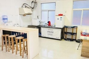 Uma cozinha com balcão, banquetas, dispensador de água e uma janela.