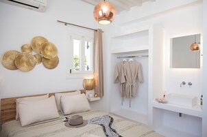 Quarto com cama, mesa de cabeceira, abajur e vista para um banheiro com pia e espelho.