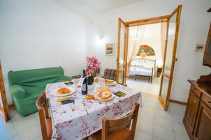 Uma área de refeições com uma mesa posta para dois, um sofá verde e uma cama com um mural colorido ao fundo.