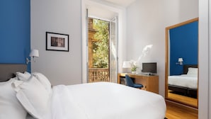 Quarto de hotel com cama, escrivaninha, televisão e varanda com vista para o verde.