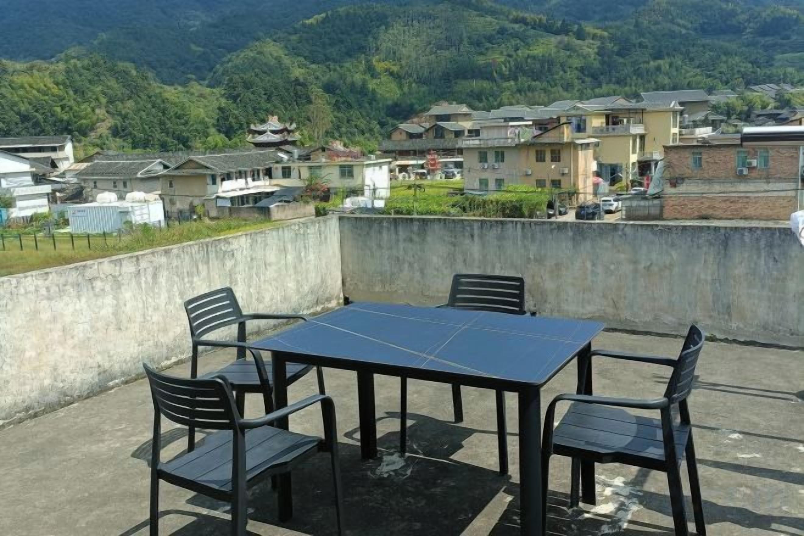 Terraço no telhado com mesa e cadeiras, com vista para uma área residencial com casas e vegetação.