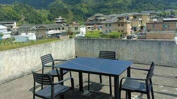 Terraço no telhado com mesa e cadeiras, com vista para uma área residencial com casas e vegetação.