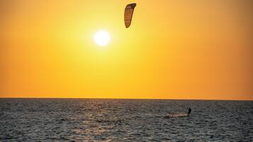 Pôr do sol sobre o oceano com uma pessoa praticando windsurf.