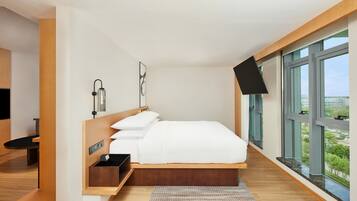 Quarto moderno com cama, mesas de cabeceira, televisão de tela plana e janelas amplas com vista para a cidade.