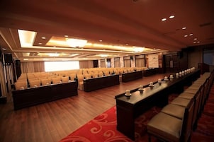 Uma sala de conferências ampla, com fileiras de cadeiras, uma mesa longa e um palco.
