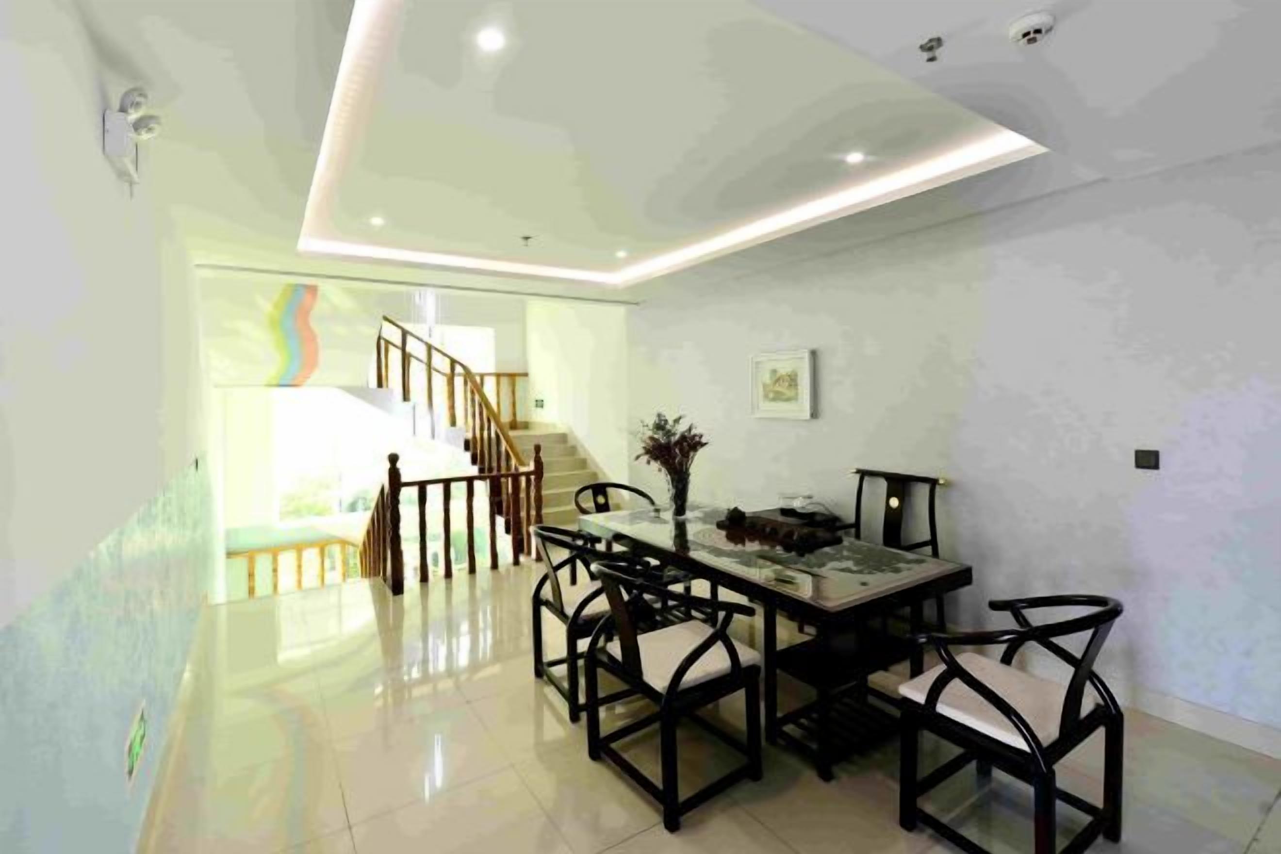 Uma área de refeições com mesa e cadeiras, escada ao fundo e teto com iluminação embutida.