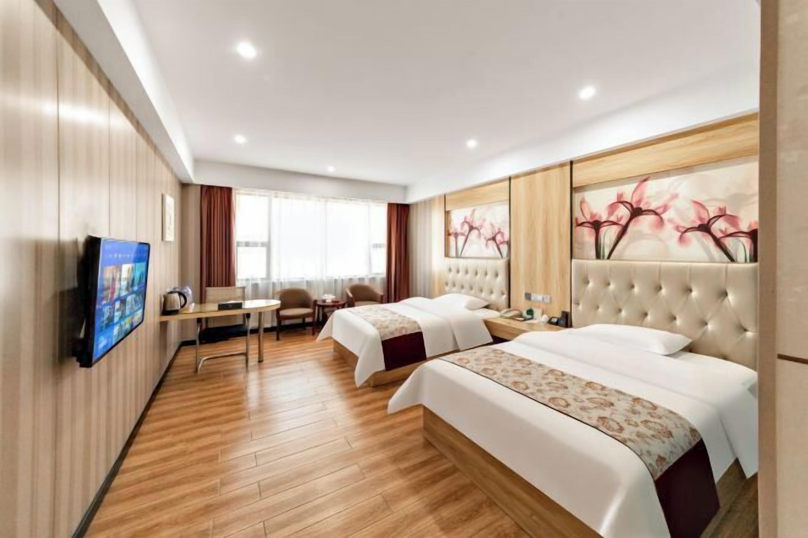 Quarto de hotel com duas camas, televisão, escrivaninha e uma cadeira.