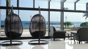 Um interior moderno com janelas amplas, duas cadeiras suspensas, um sofá e vista para o mar.