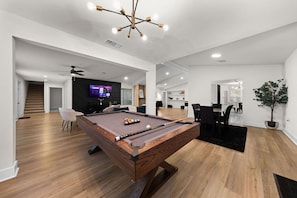 Uma sala de estar moderna com mesa de bilhar, televisão de tela plana e área de jantar com mesa e cadeiras pretas.