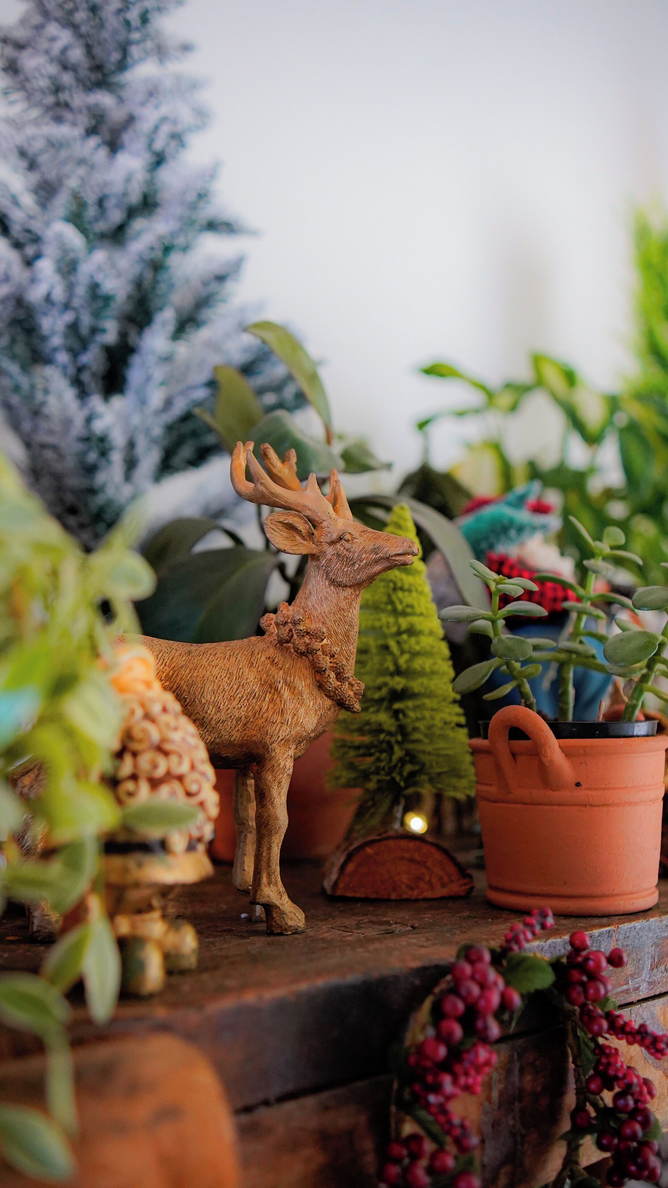 Uma estatueta de veado, um pequeno pinheiro de Natal e vários vasos com plantas sobre uma superfície de madeira.