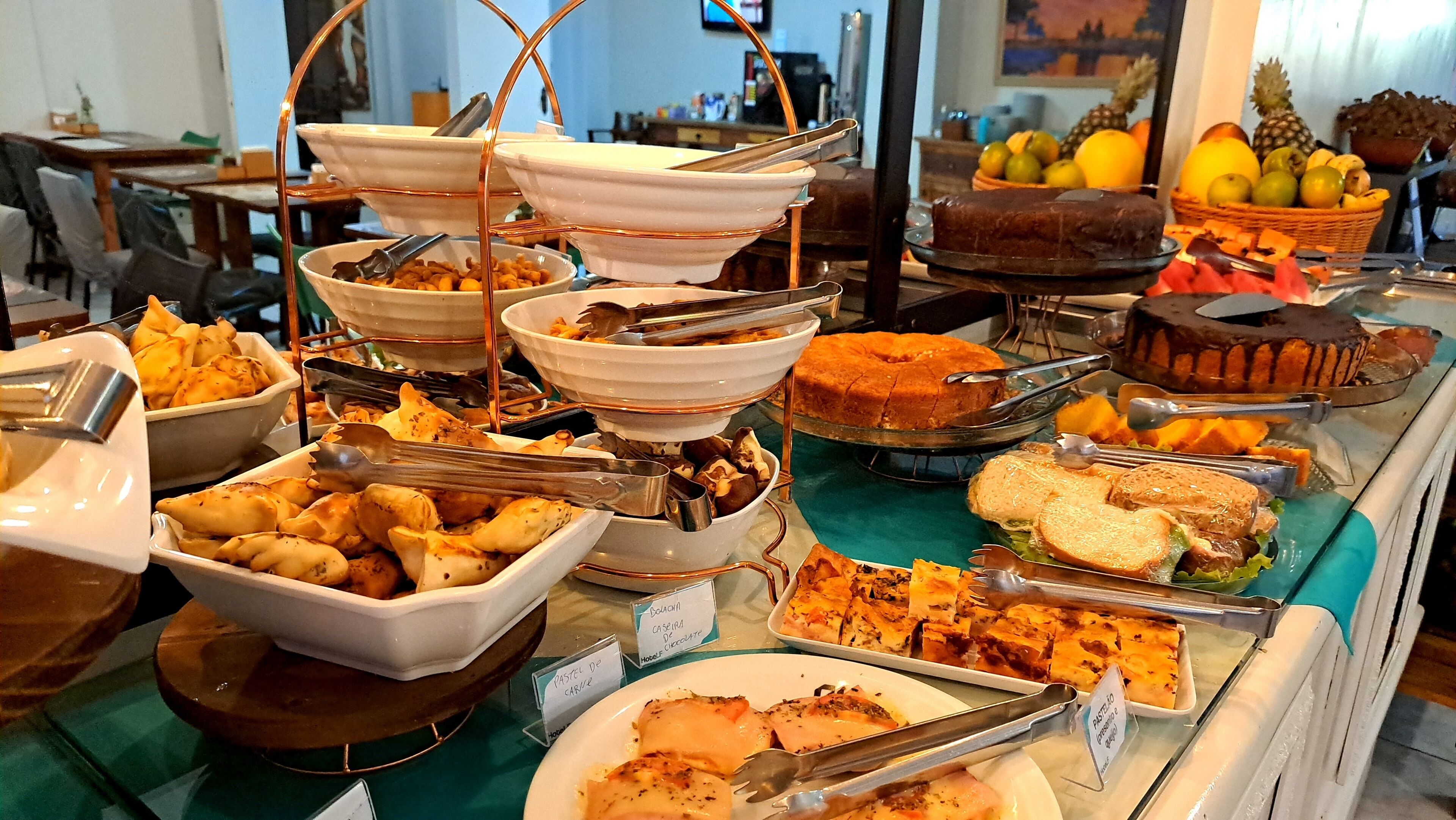 Buffet com diversos itens, incluindo doces, sanduíches e uma cesta de frutas.