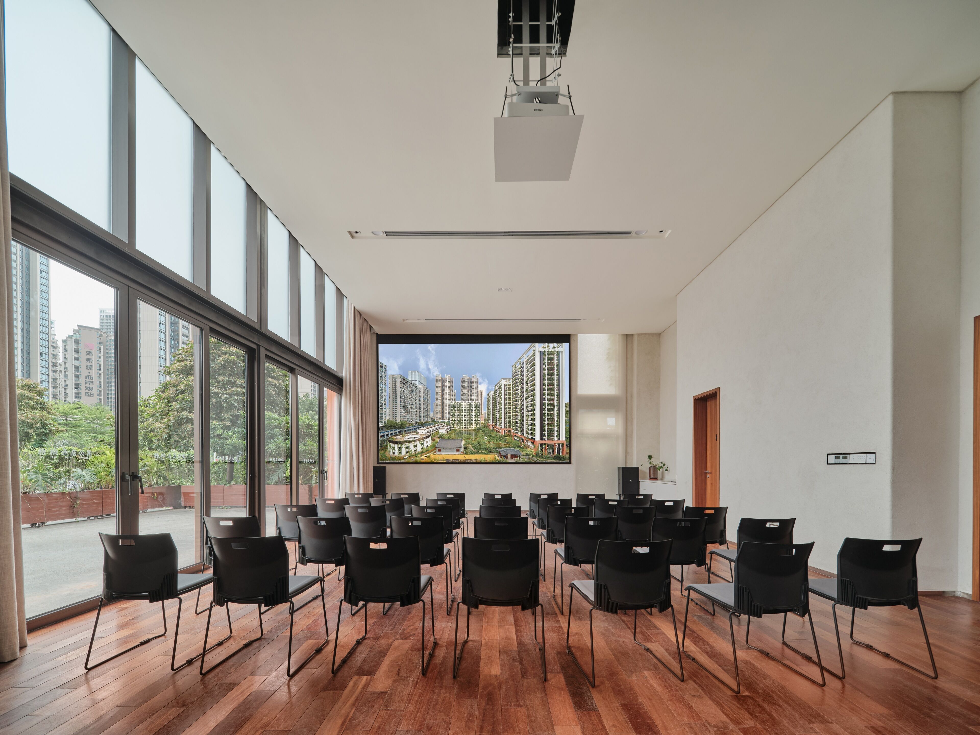 Uma sala de conferência com uma janela grande, cadeiras pretas e um projetor.