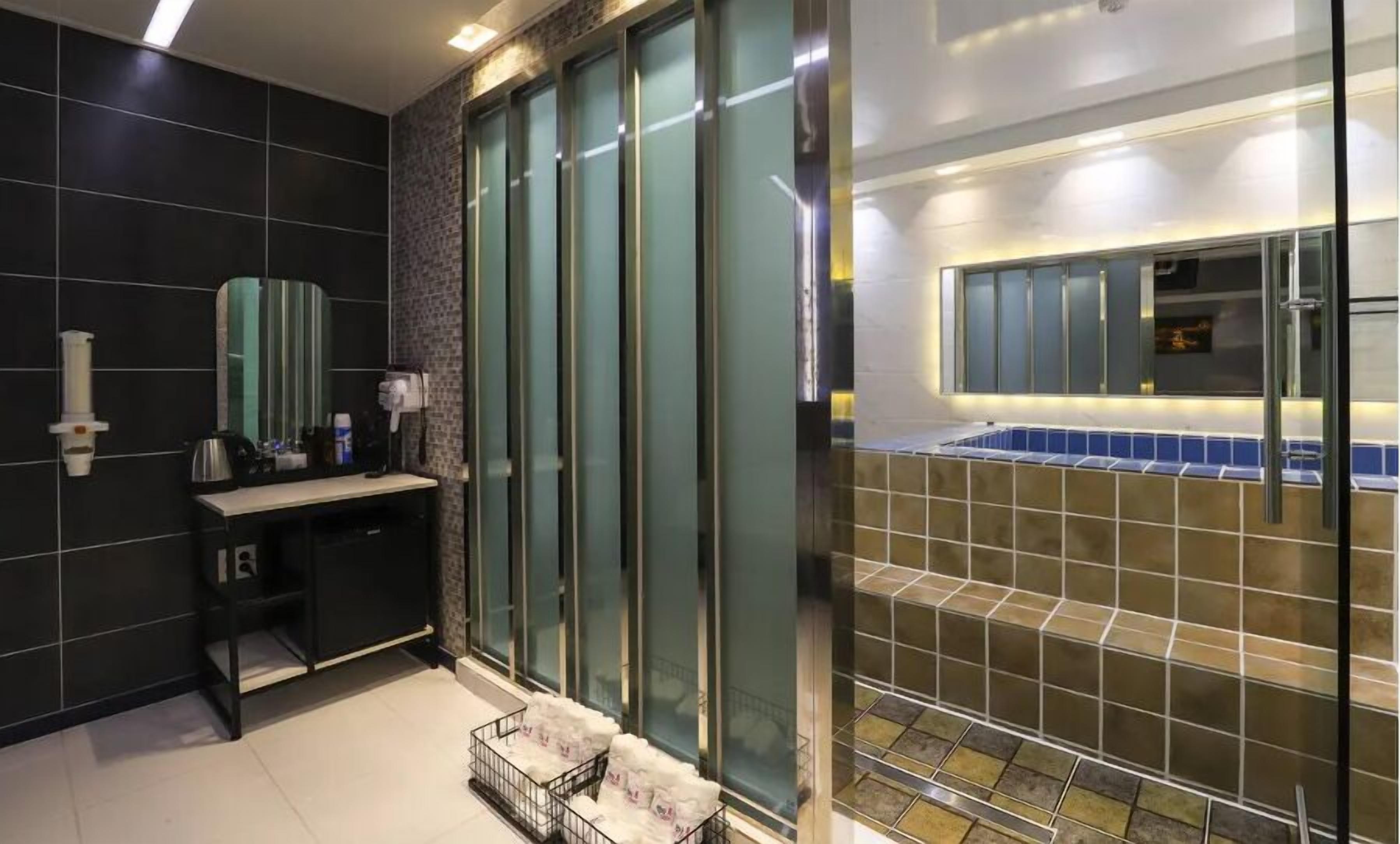 Um banheiro moderno com azulejos escuros, um espelho grande, box de vidro e piso ladrilhado.