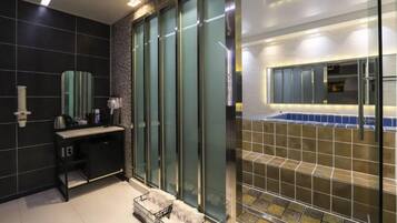 Um banheiro moderno com azulejos escuros, um espelho grande, box de vidro e piso ladrilhado.
