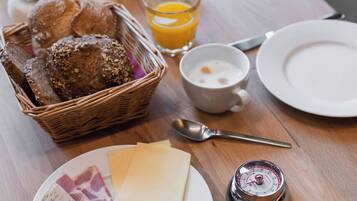 Mesa de café da manhã com pão, queijo, presunto, uma xícara de café, um copo de suco de laranja e uma garrafa térmica.