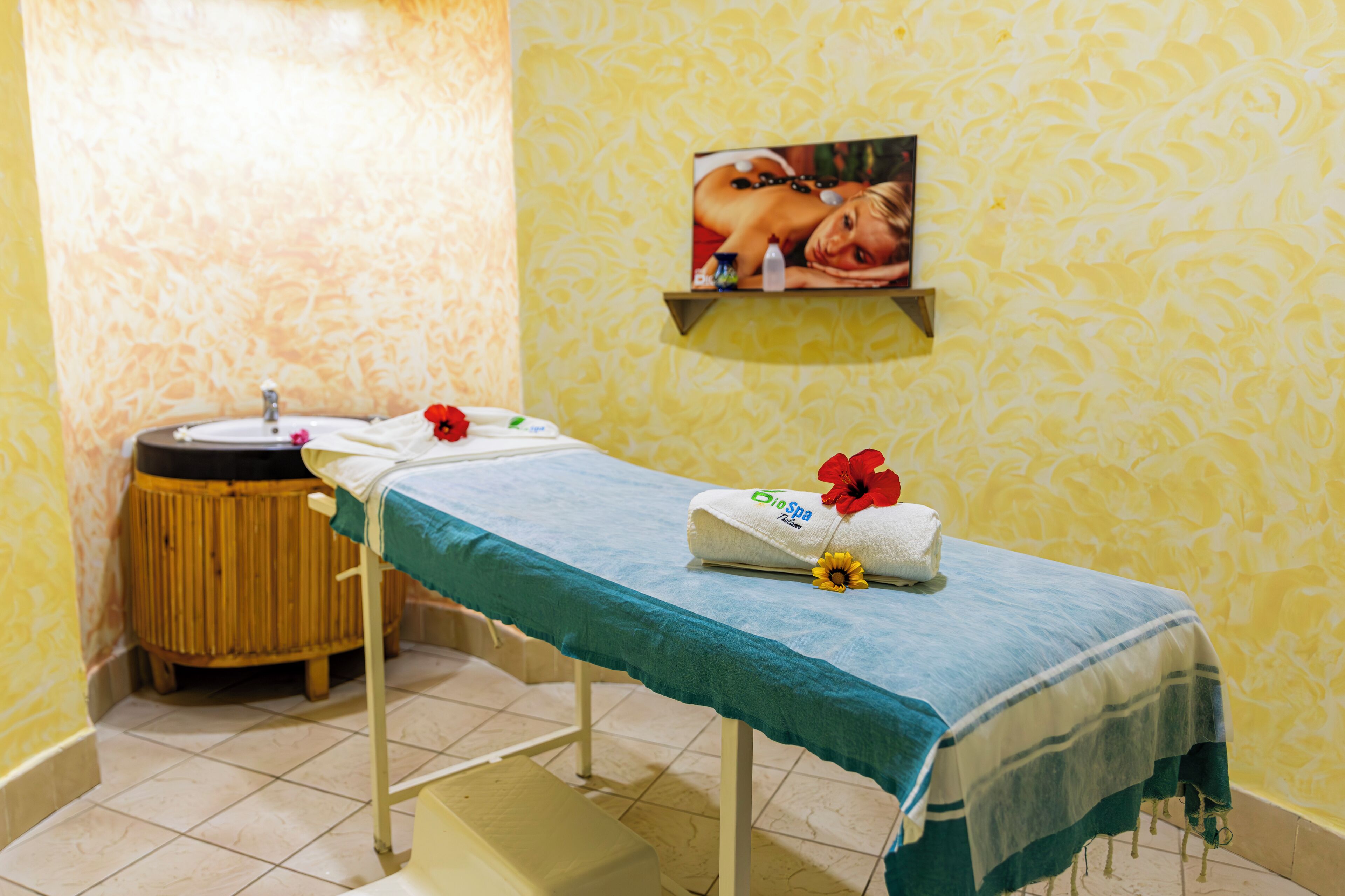 Um espaço de spa com mesa de massagem, pia e um banquinho de madeira.