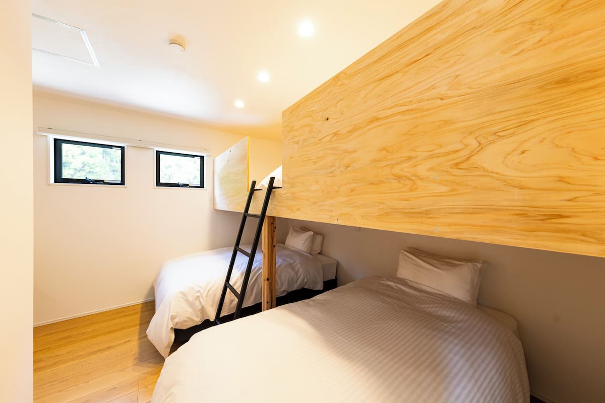 Quarto com cama beliche, escada e duas janelas.