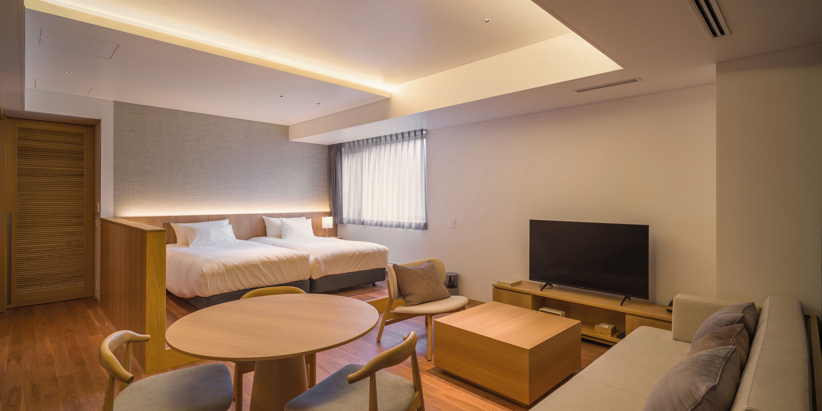 Quarto de hotel com duas camas, televisão, mesa de jantar e sofá.
