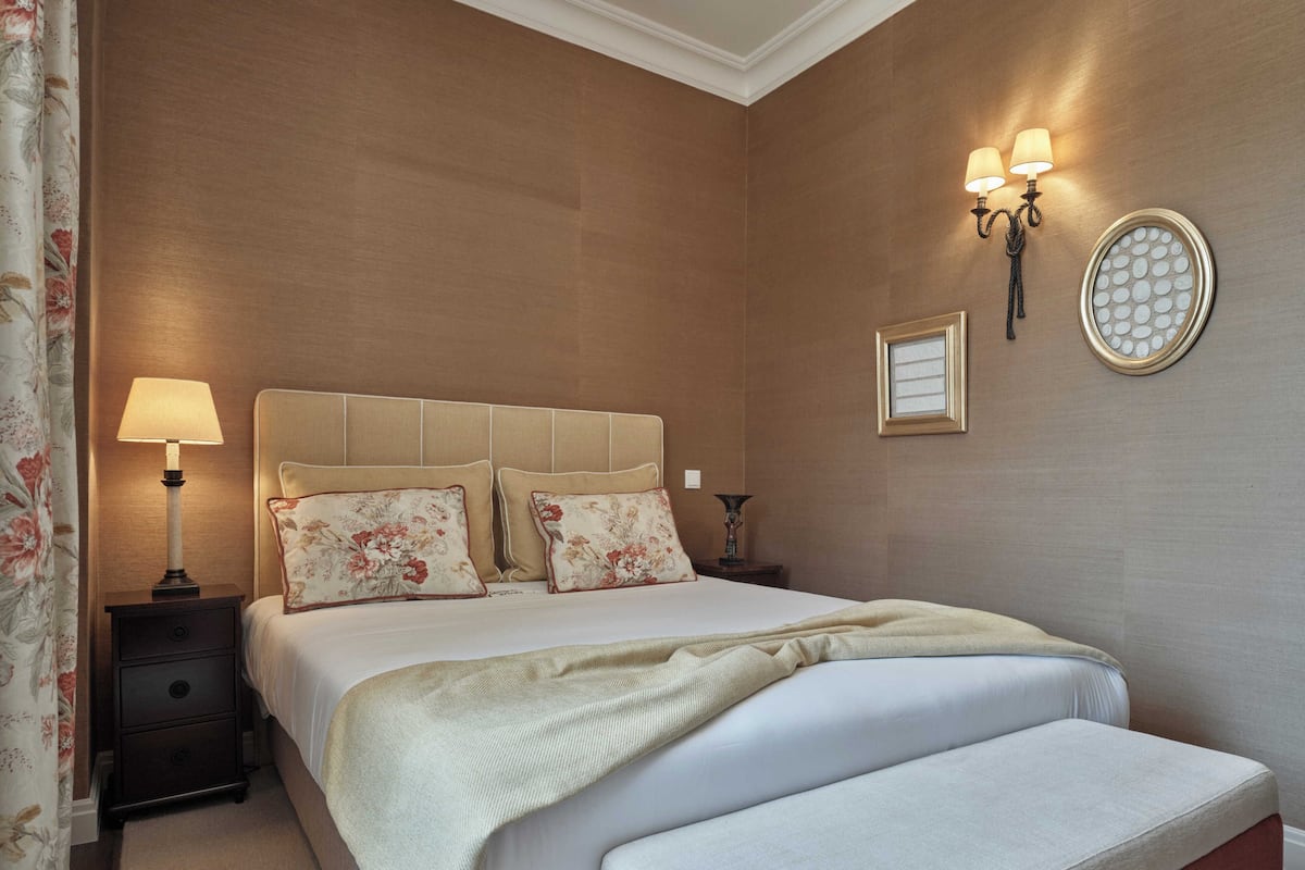 Quarto bem arrumado com cama, abajures, mesa de cabeceira e luminária na parede.