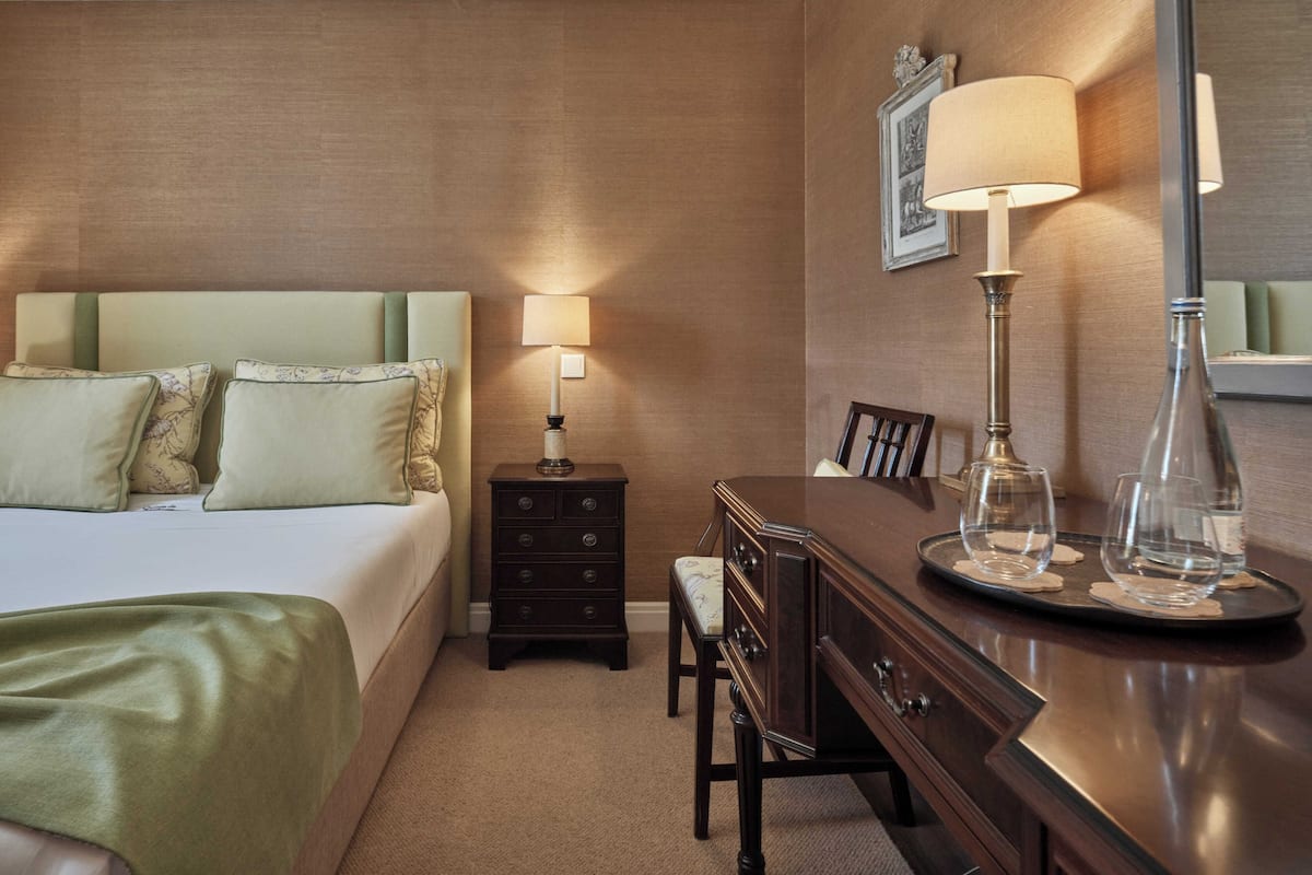 Quarto de hotel com uma cama, uma mesa de cabeceira com abajur, cômoda e espelho.
