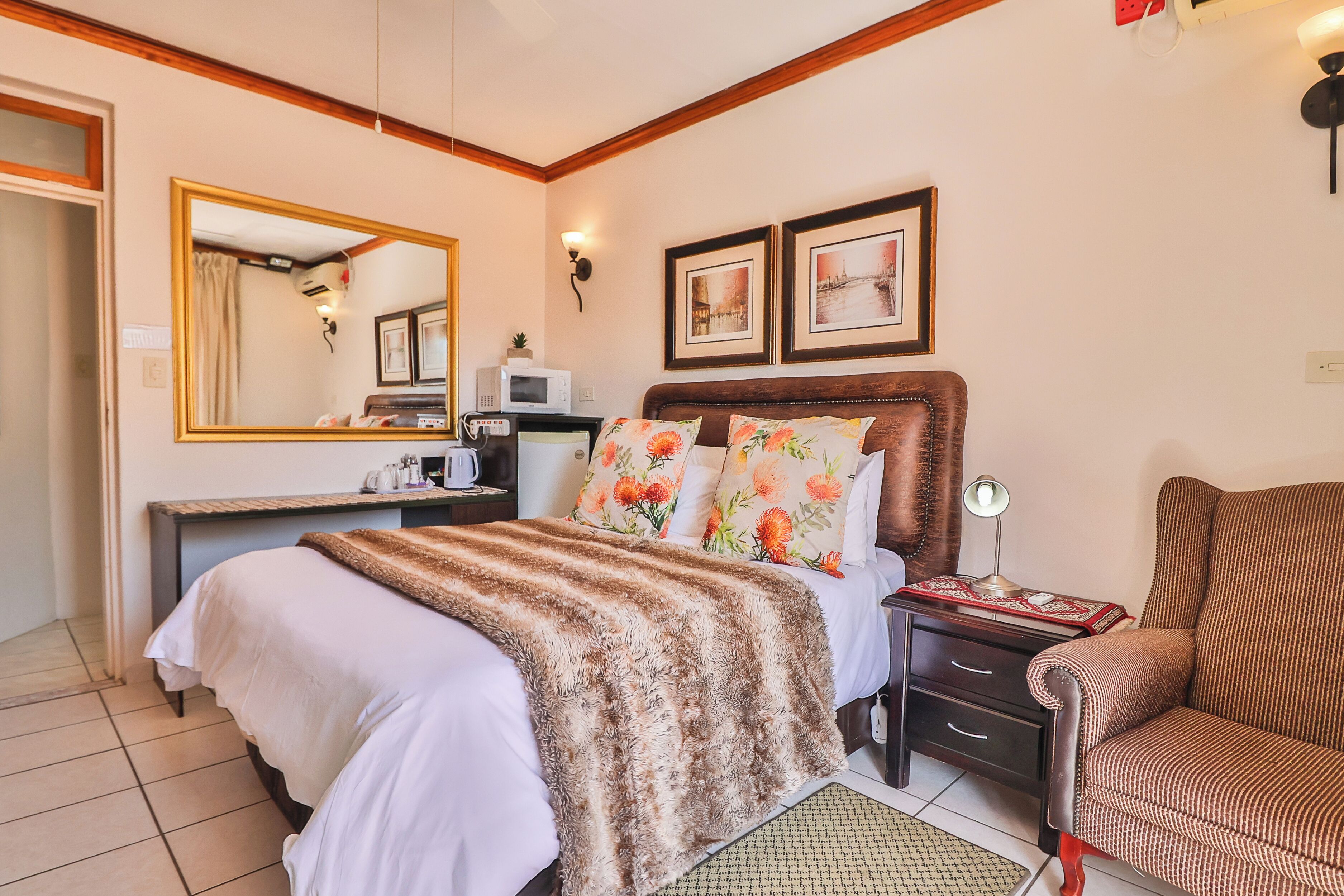 Um quarto com cama, mesa de cabeceira, abajur, cadeira e espelho.