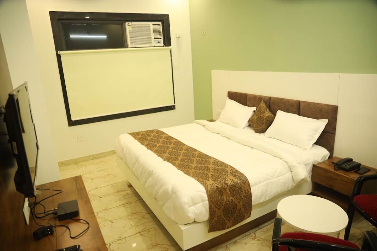 Quarto de hotel com cama, mesa de cabeceira com telefone, pequena mesa redonda e televisão sobre suporte.