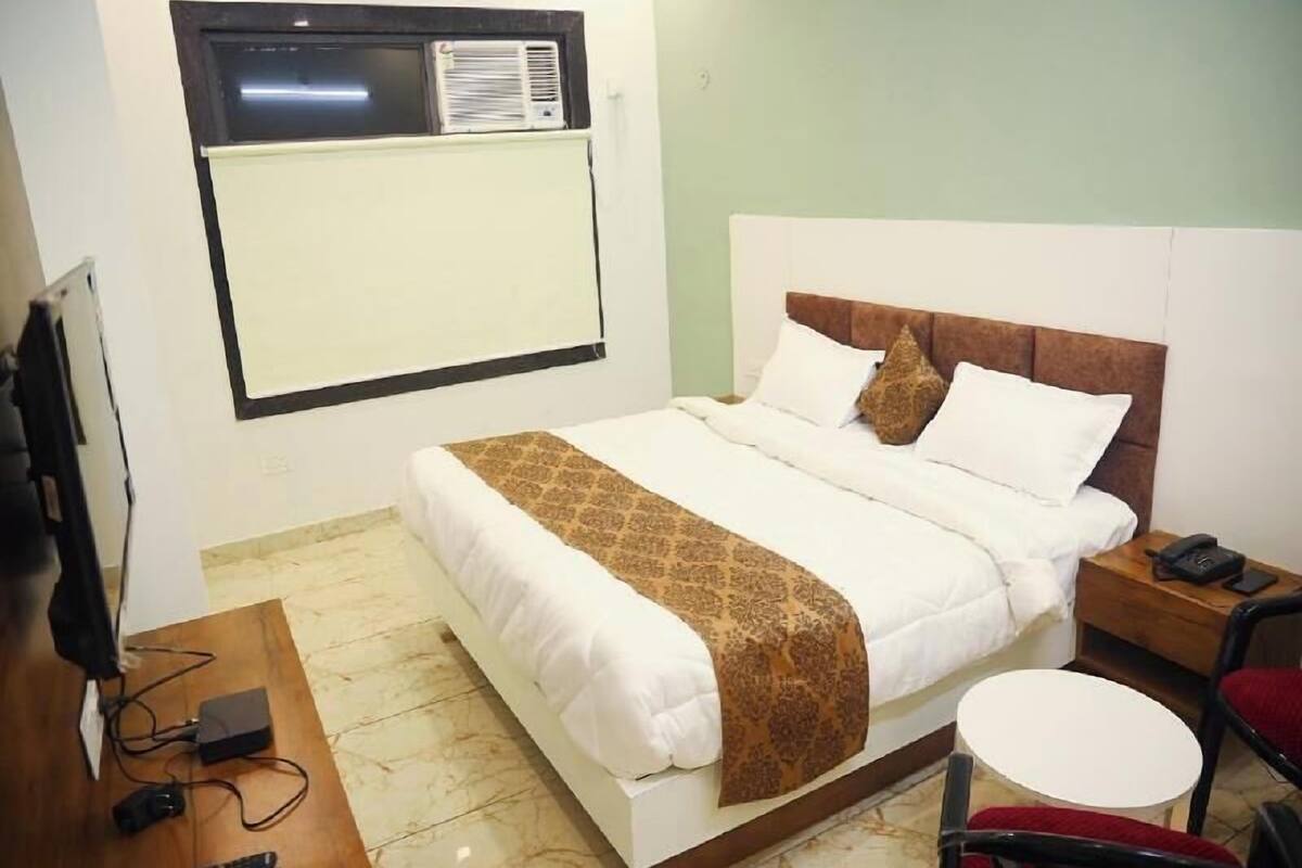Quarto de hotel com cama, mesa de cabeceira, cadeira e televisão.